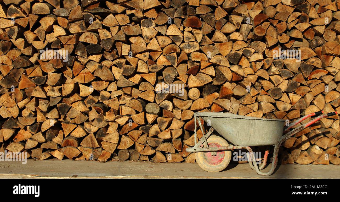 Wheelbarrow In Front Of Fuelwood Stack At Sunny Day Stock Photo - Alamy