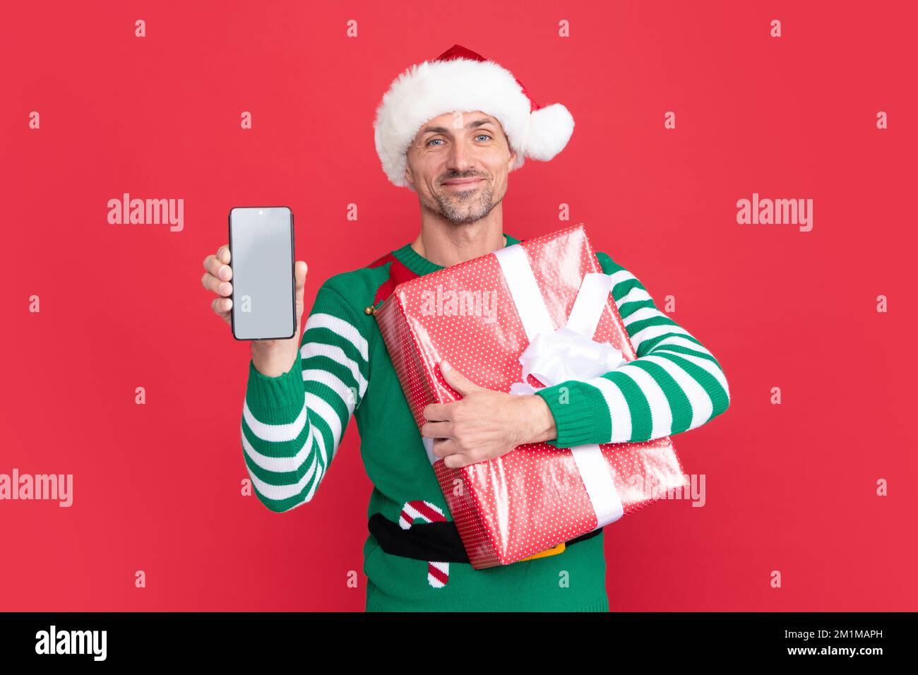 happy man showing phone screen. man in elf costume and santa claus hat ...