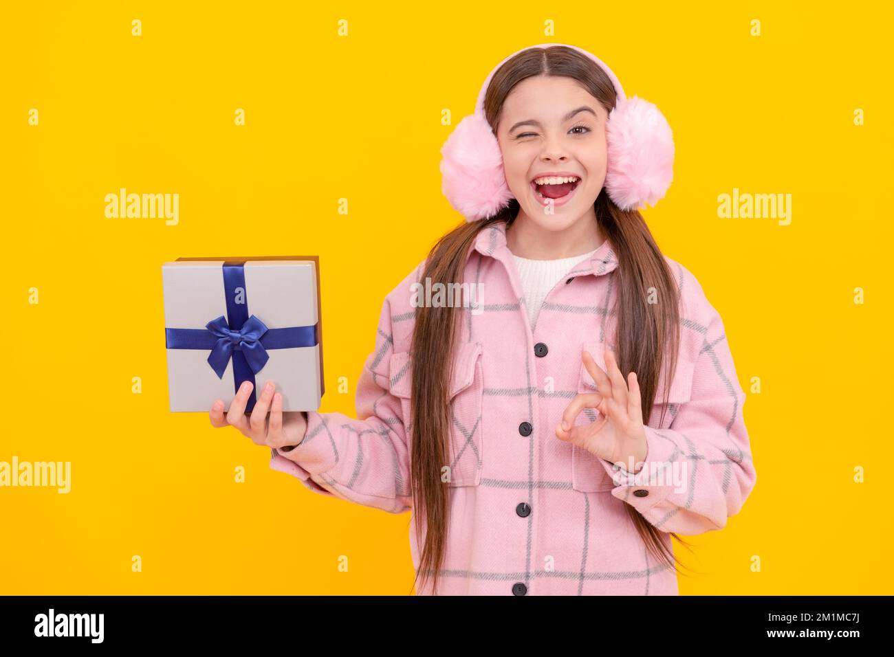 Happy winking kid hold present gift box showing ring gesture yellow ...