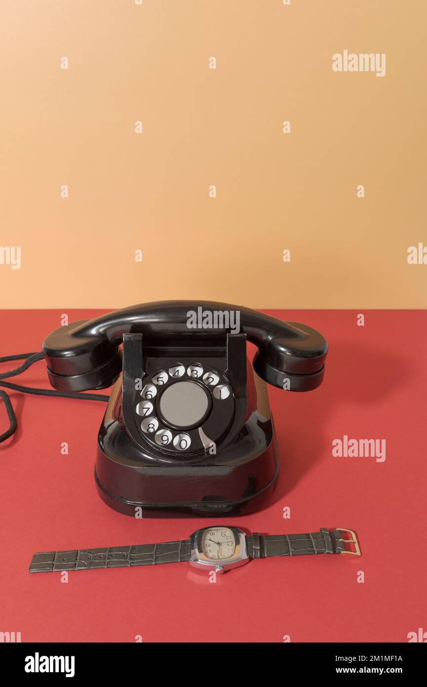Retro phone from 60s 70s and retro watch with leather strap. On a red ...