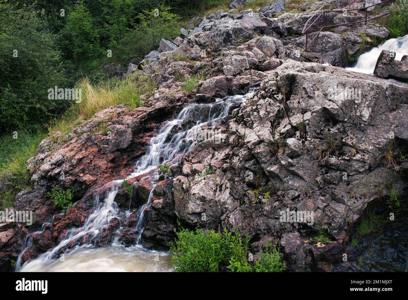 A small waterfall flowing over rocks in a wooded area with trees in the ...