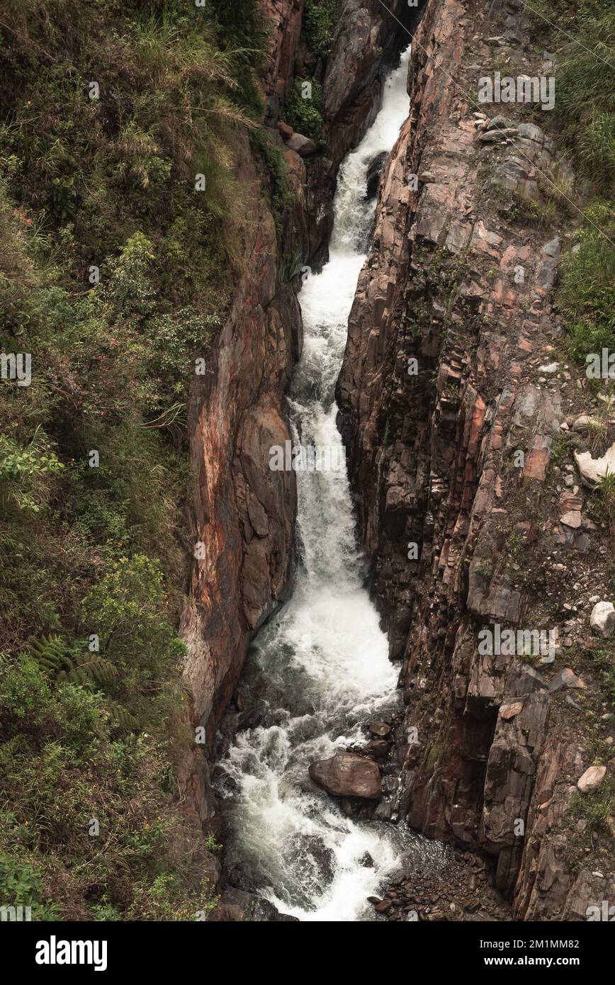 A vertical shot of a waterfall flowing through narrow rocks near Banos ...