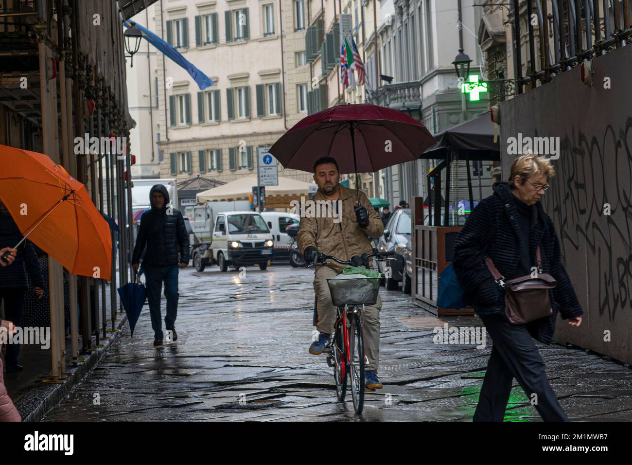 Cycling in the rain in Florence with an umbrella Stock Photo - Alamy