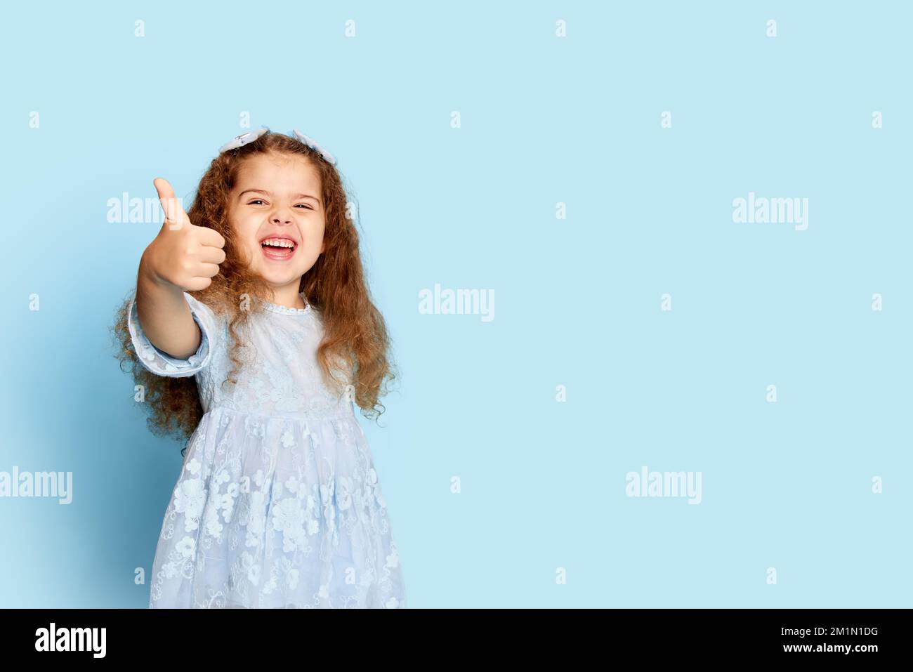 Nice, good sign. Studio shot of preschool age girl in blue dress thumbs ...