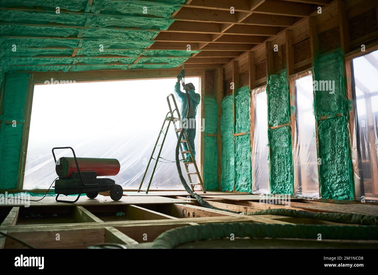 Male builder insulating wooden frame house. Man worker spraying ...