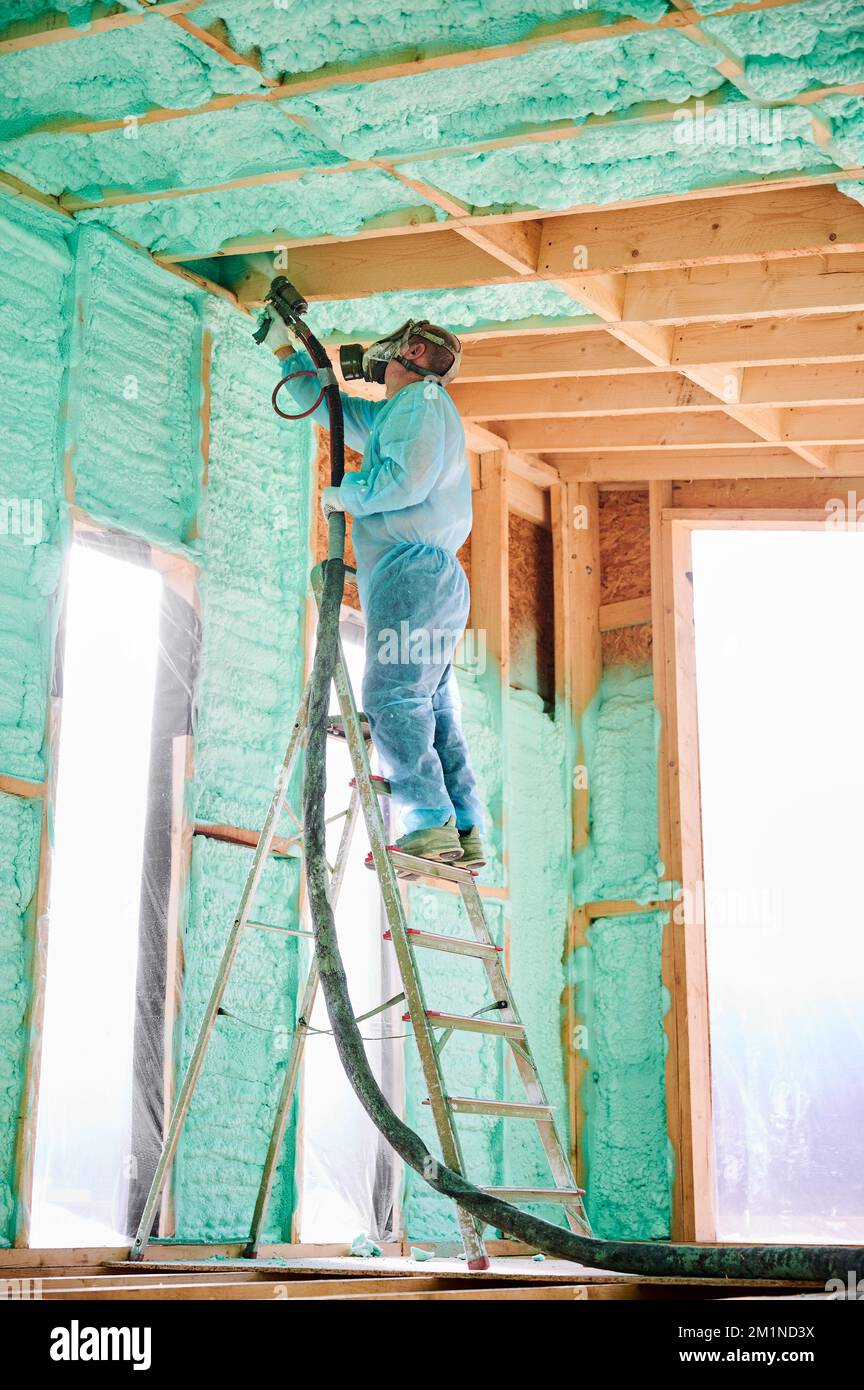 Male builder insulating wooden frame house. Man worker spraying ...