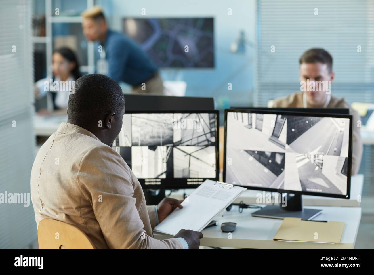 Back view of man looking at surveillance camera feeds at screen in ...