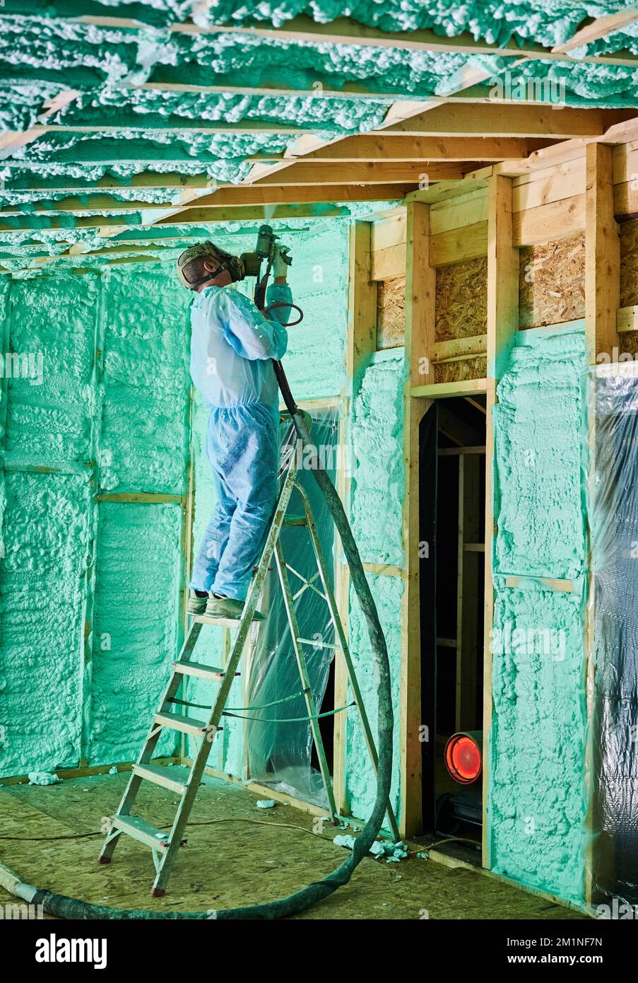 Male builder insulating wooden frame house. Man worker spraying ...