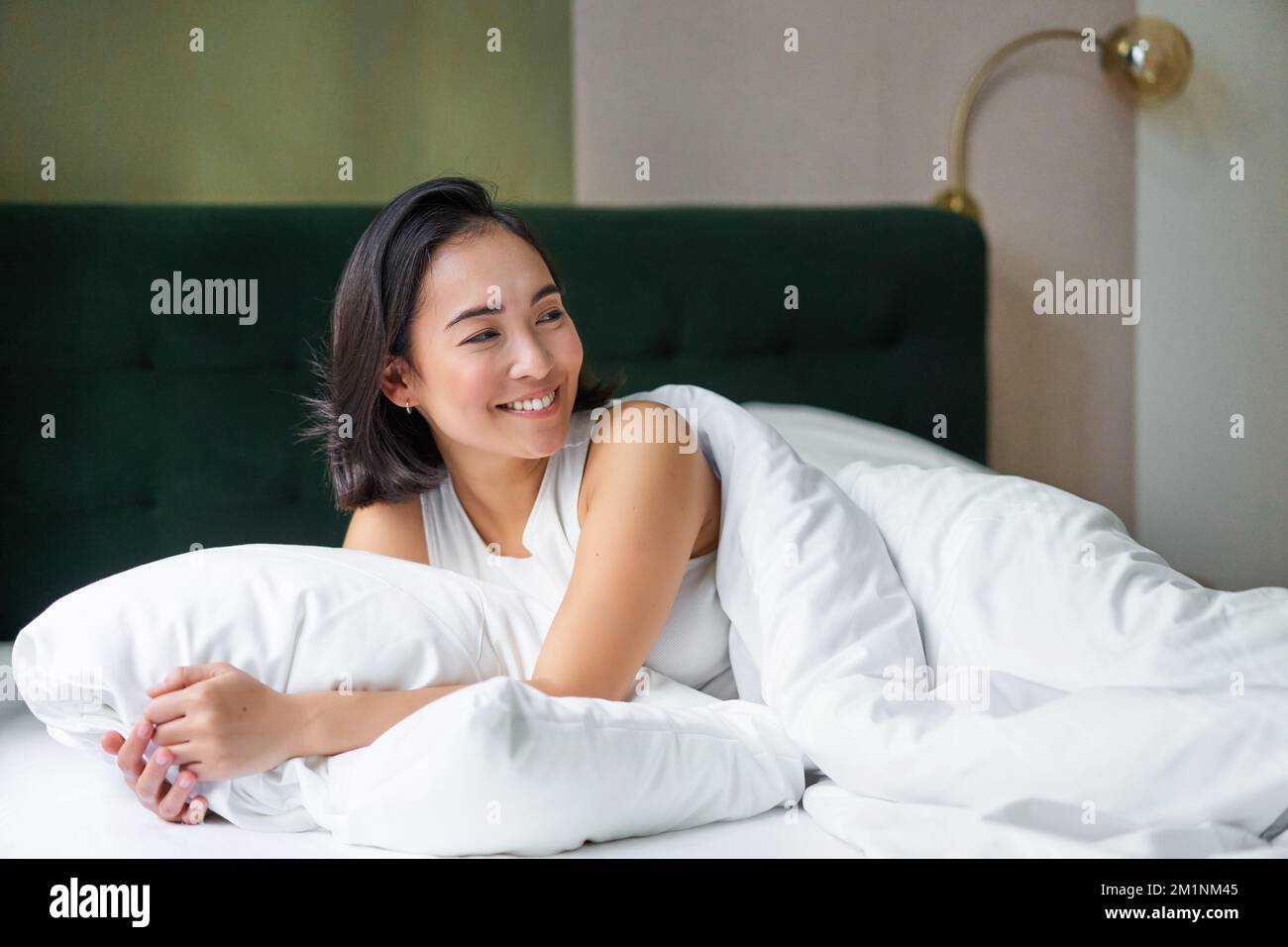 Happy mornings. Beautiful korean woman lying in bed, smiling, waking up ...