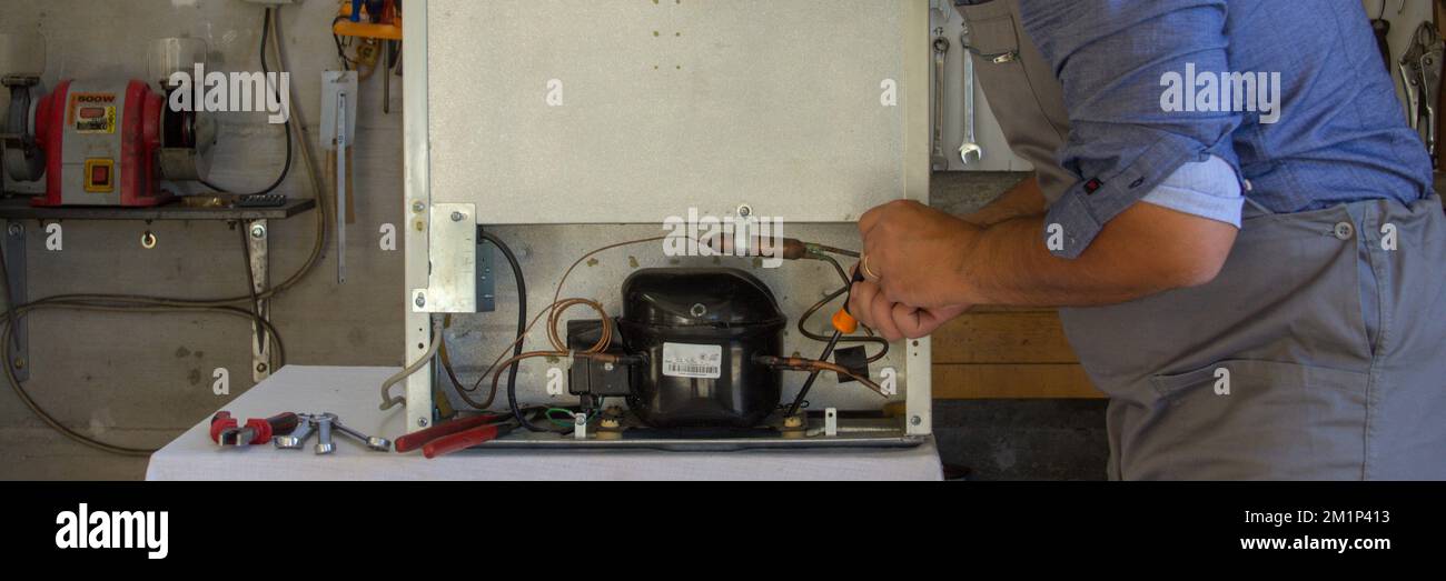 Image of a handyman technician in his workshop repairing a refrigerator ...