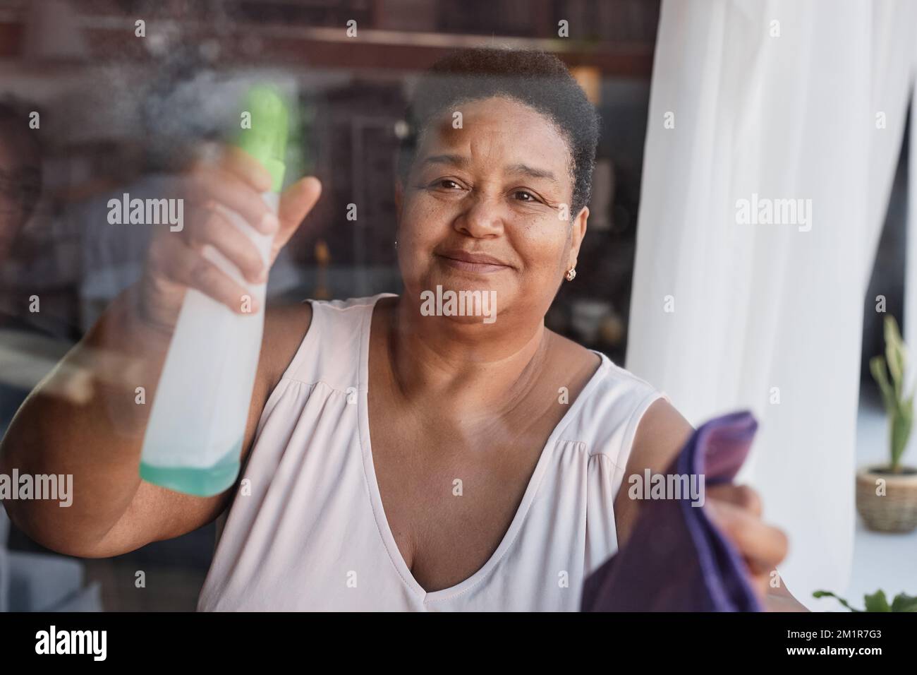 Portrait of black senior woman cleaning windows at home and smiling ... Portrait of black senior woman cleaning windows at home and smiling ...