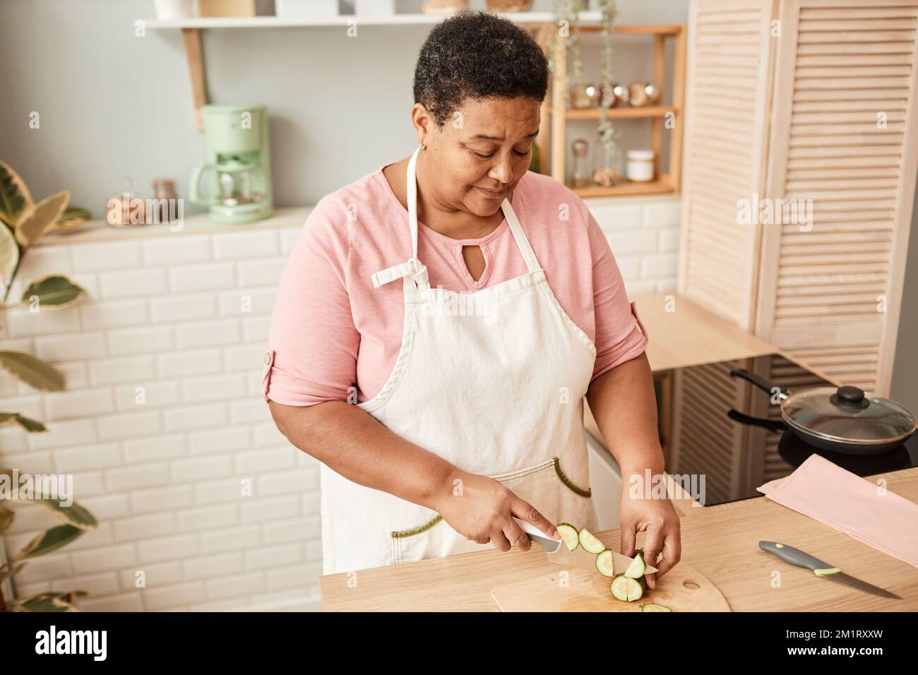 High angle portrait of black senior woman cutting vegetables in cozy ...