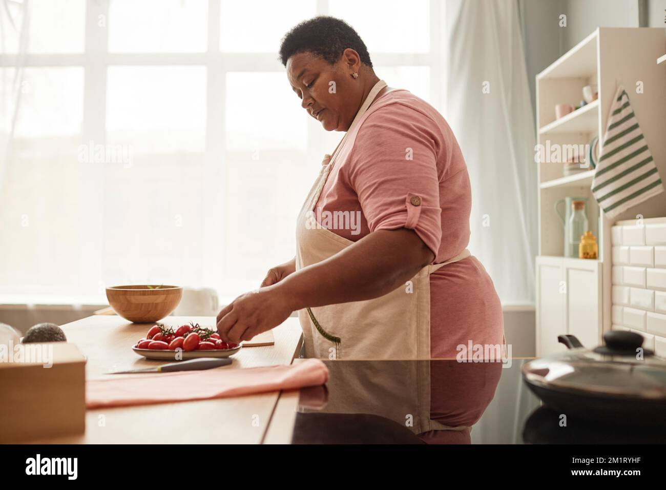 Side view at black senior woman wearing apron while cooking in cozy ...
