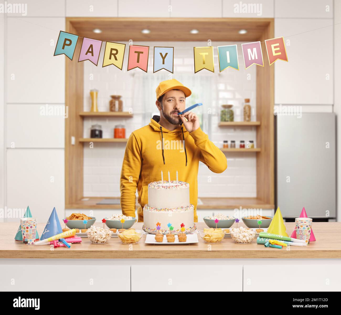 Casual young man preparing for a party and blowing a party horn behind ...