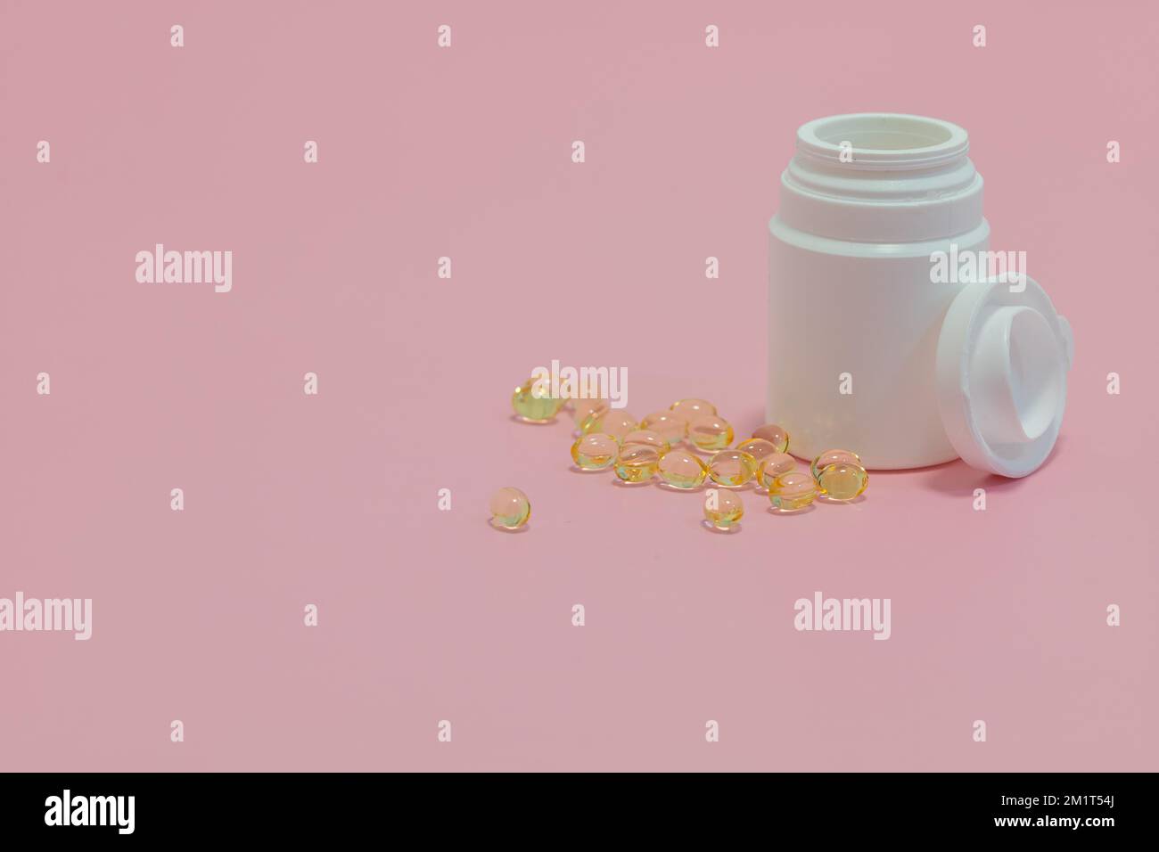 A closeup shot of a white pill container and yellow capsules on a pink ...