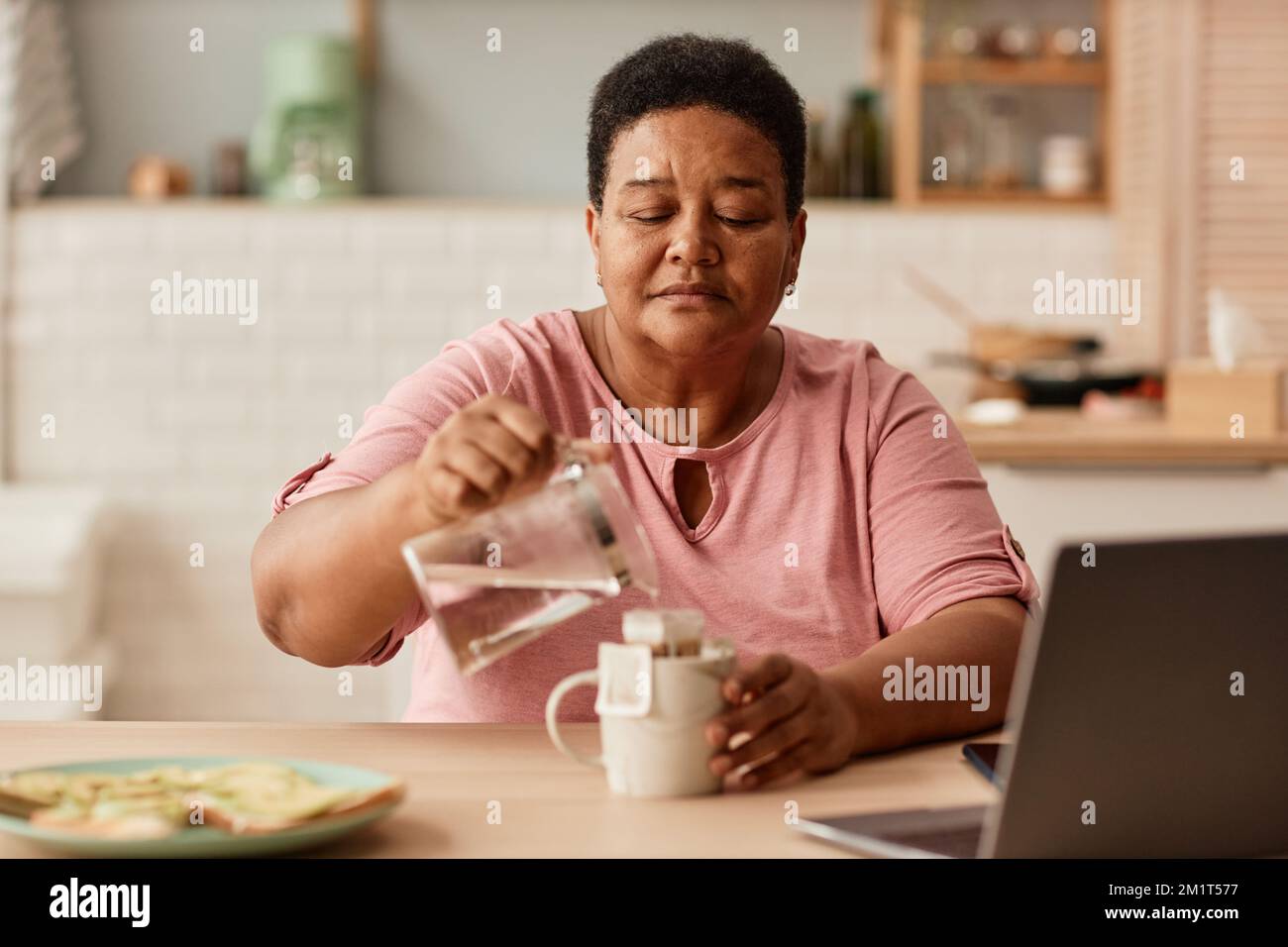 Warm toned portrait of black senior woman making tea during breakfast ...