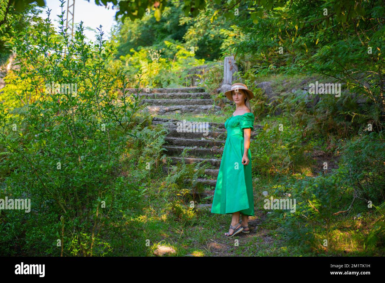 A girl in a green dress and a hat at the steps in greenery Stock Photo ...