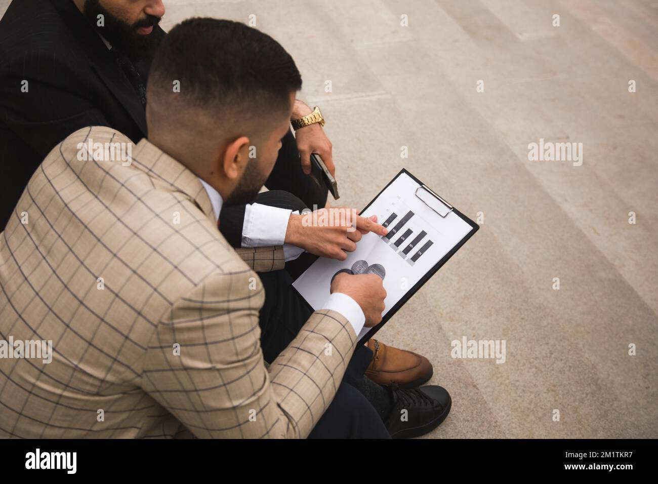 Business people outdoor meeting. Several men in suits sit on the steps ...