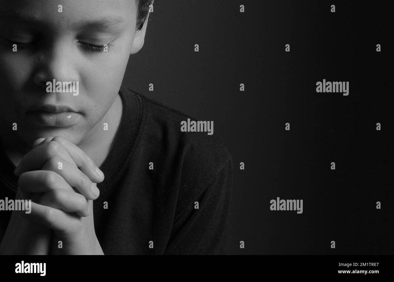 little boy praying to God with hands together with black background ...