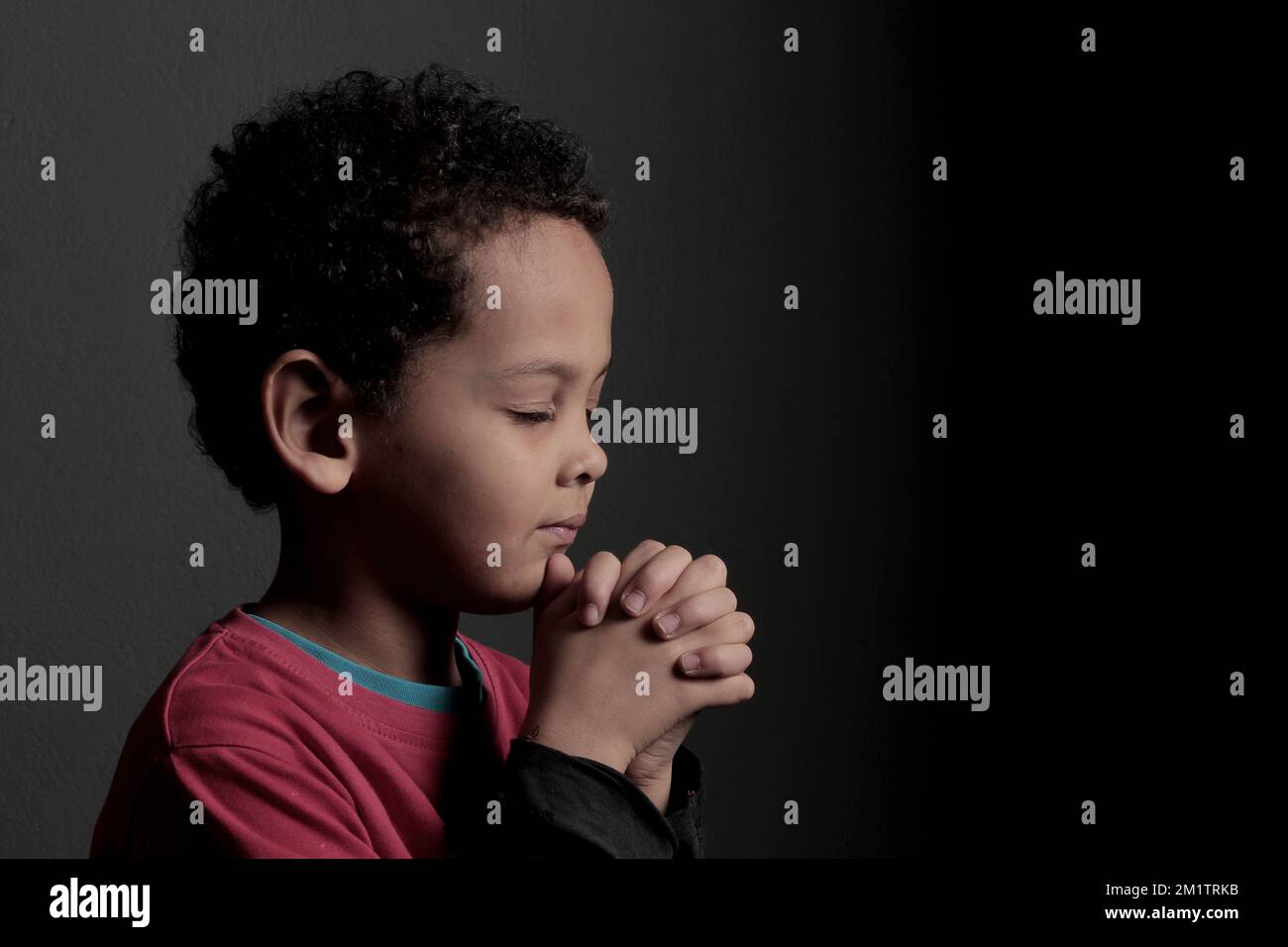 little boy praying to God with hands together with black background ...