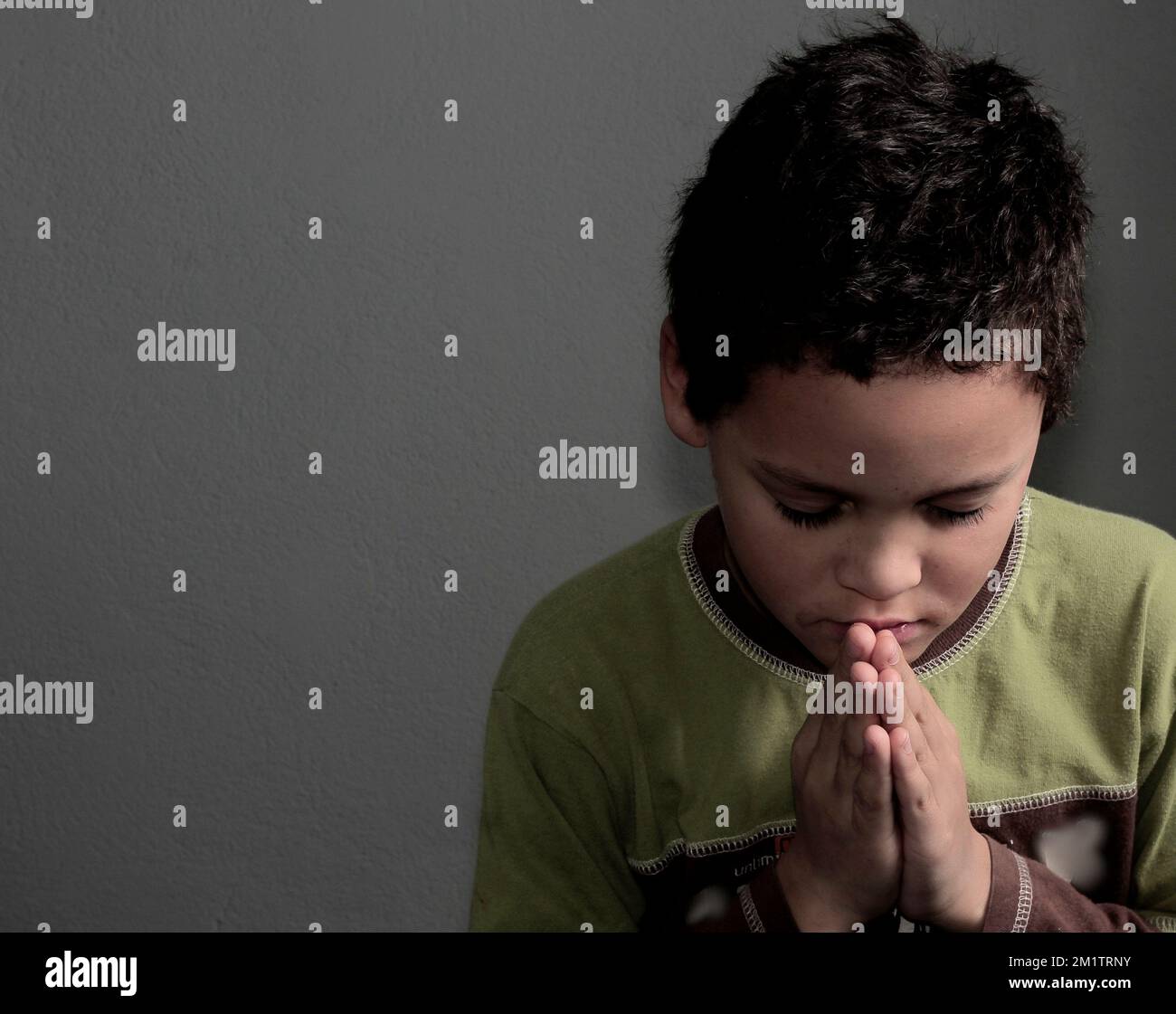 little boy praying to God with hands together with black background ...