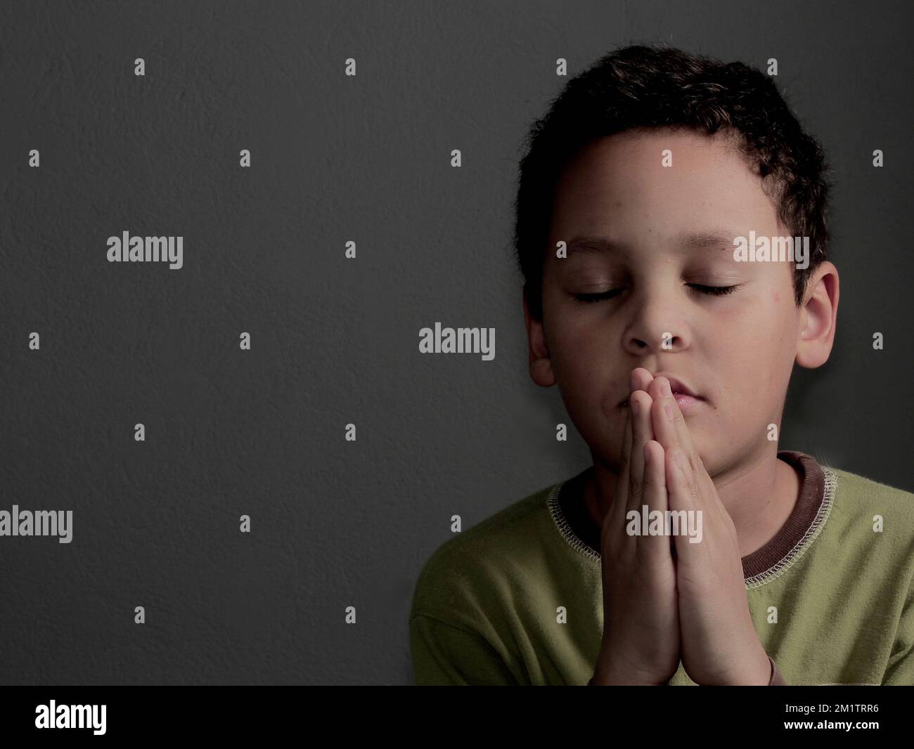 little boy praying to God with hands together with black background ...