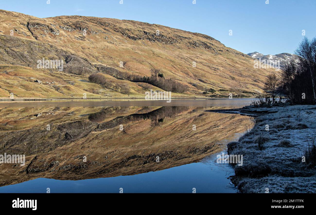 Reflections on Loch Lubhair showing ice on the loch with a clear, blue ...