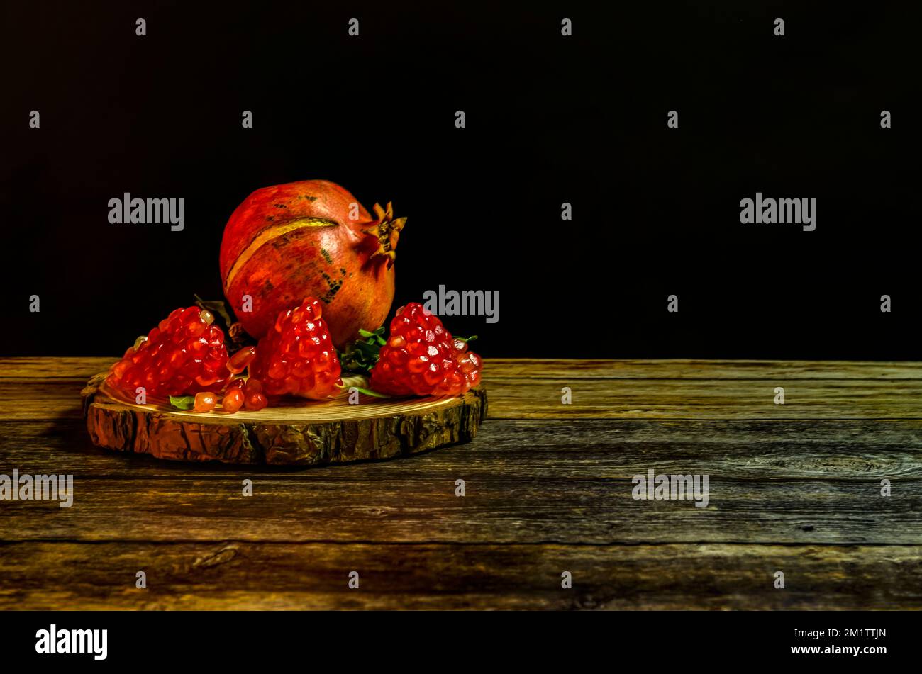 Still life of pomegranates, on a wooden table and a black background ...