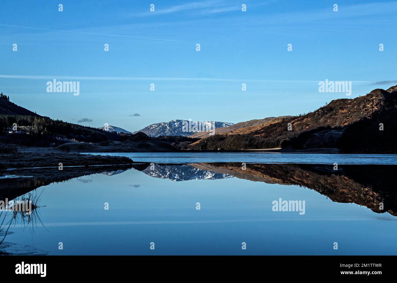 Reflections on Loch Lubhair showing ice on the loch with a clear, blue ...