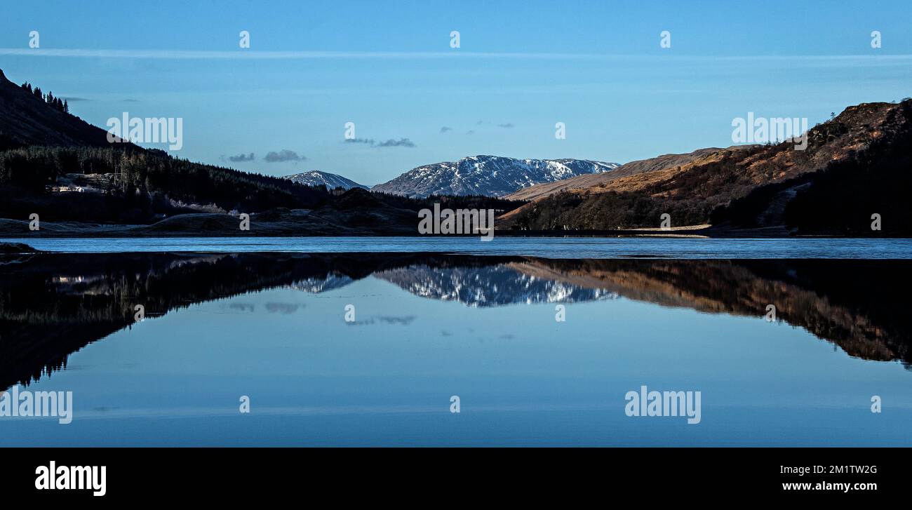 Reflections on Loch Lubhair showing ice on the loch with a clear, blue ...