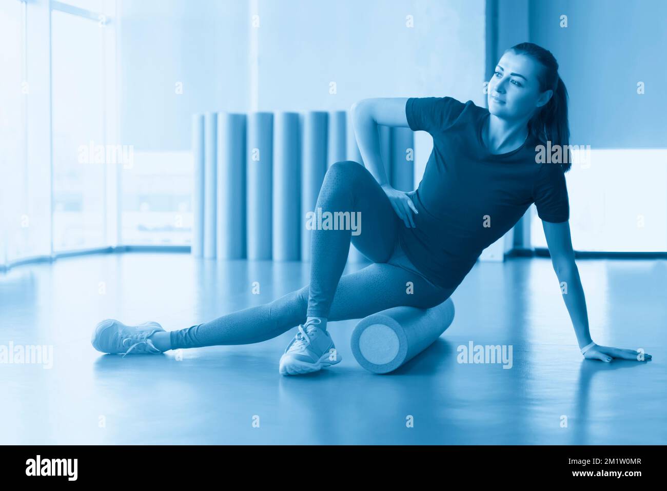 Attractive female doing foam roller exercise and posing in modern ...