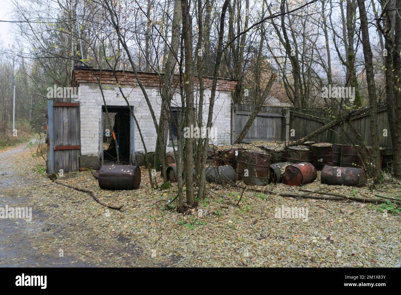 Rusty and corroed oil barrels over ground in front of a small white ...