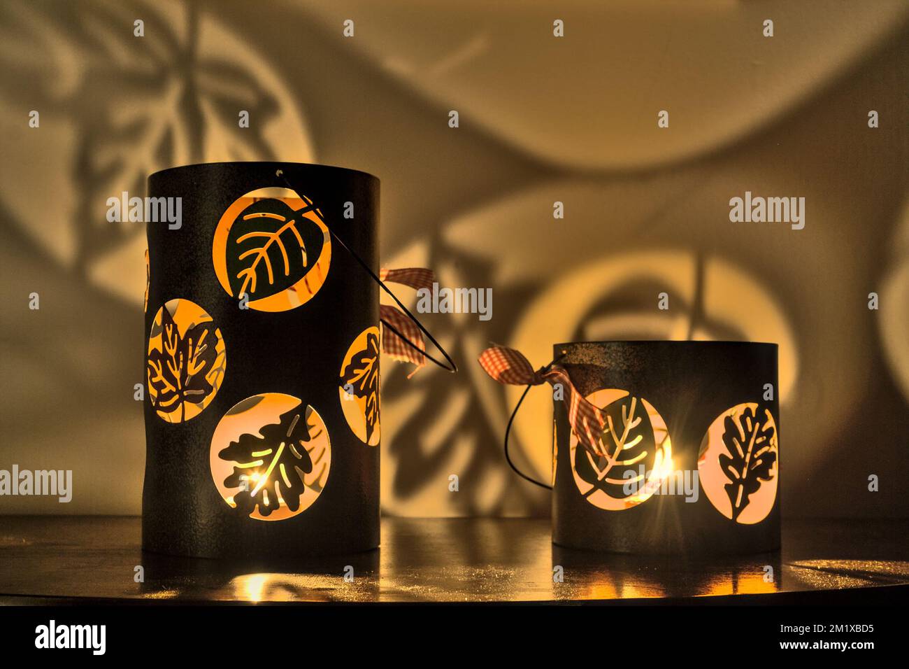 The two lit candles of different sizes with leaf-shaped cutouts in a ...