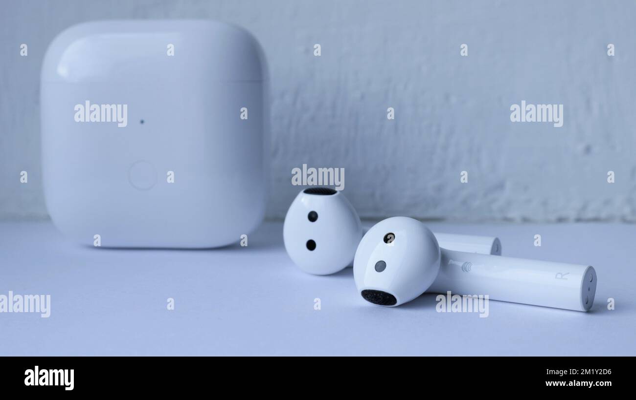 white wireless headphones and a plastic square charging box against a ...