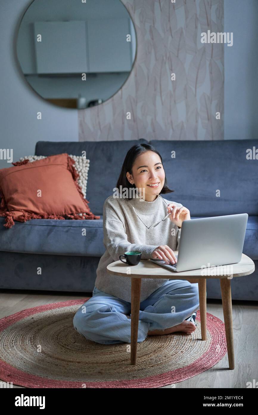 Vertical shot of korean working woman, sitting on floor at home with ...