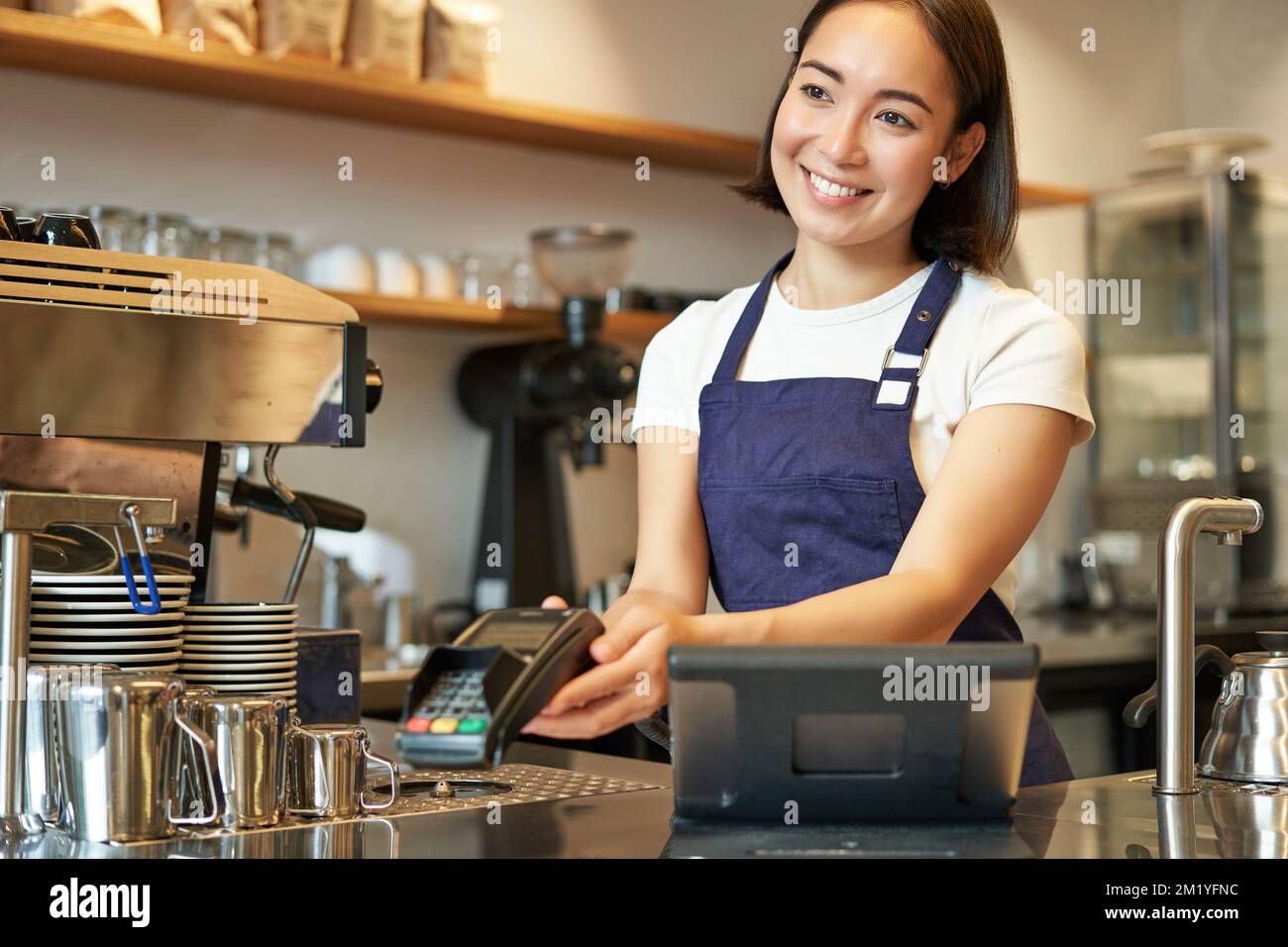 Smiling asian girl barista, giving client POS terminal, help pay with ...