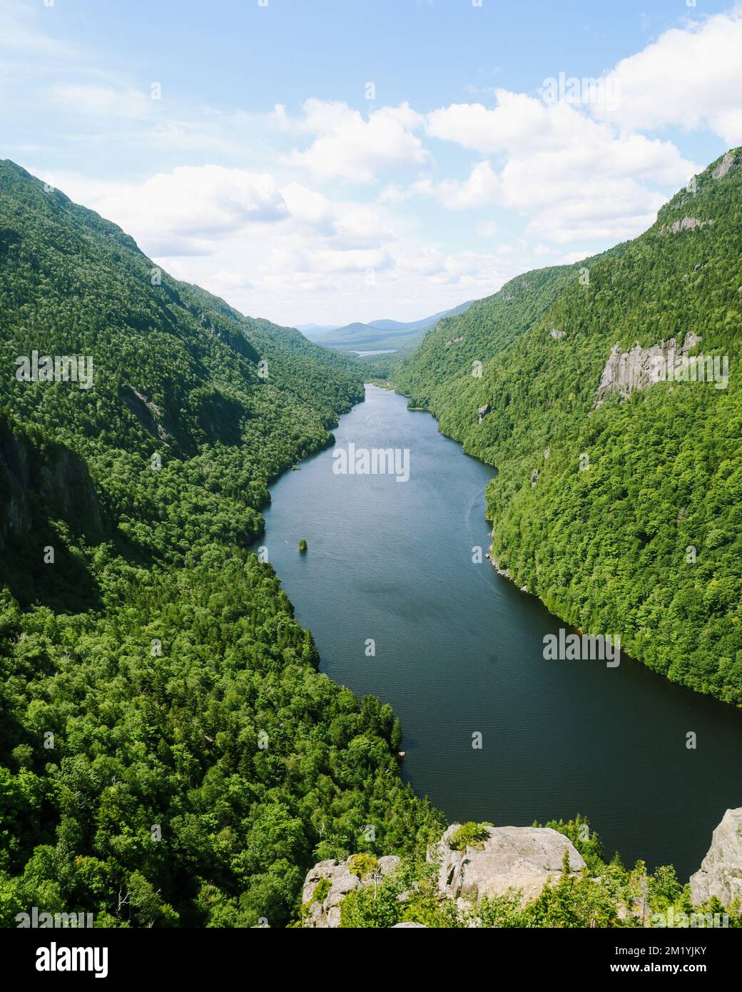 A river valley surronded by bright green trees and mountains on either ...