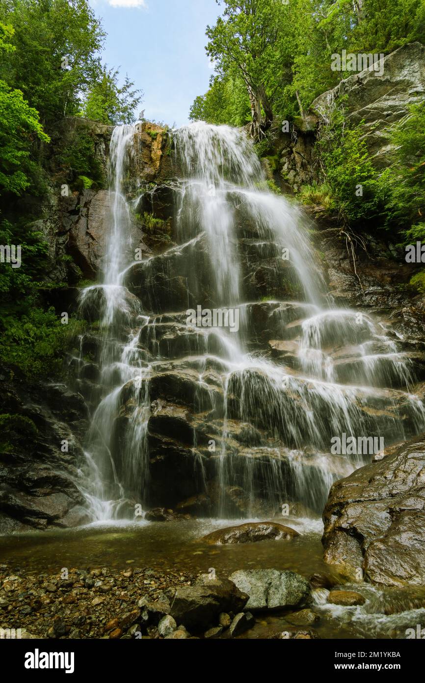 A waterfall coming down over a large cliff surrounded by green trees ...