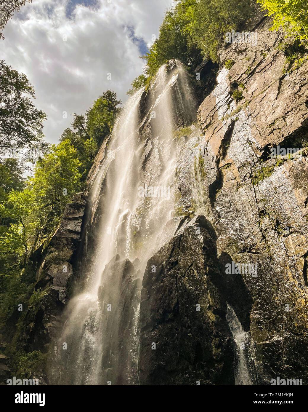 A waterfall coming down over a large cliff surrounded by green trees ...