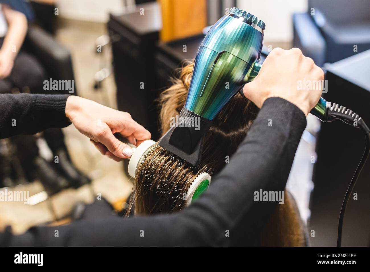 Master woman hairdresser dries the girl's hair with a hairdryer and ...