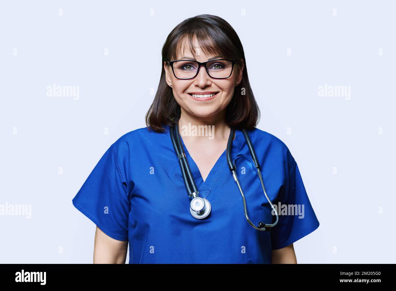 Middle aged female nurse in blue uniform with stethoscope smiling ...