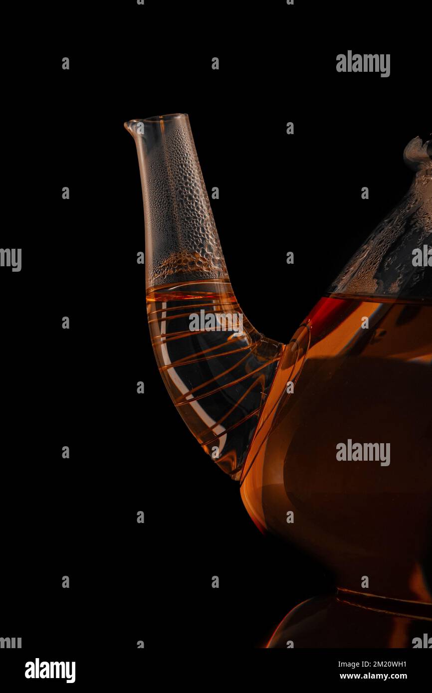 Spout of beautiful transparent glass teapot with tea close-up isolated ...