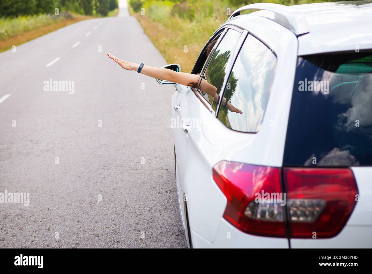 A young girl driving a car pulling her hand out of the window stops the ...
