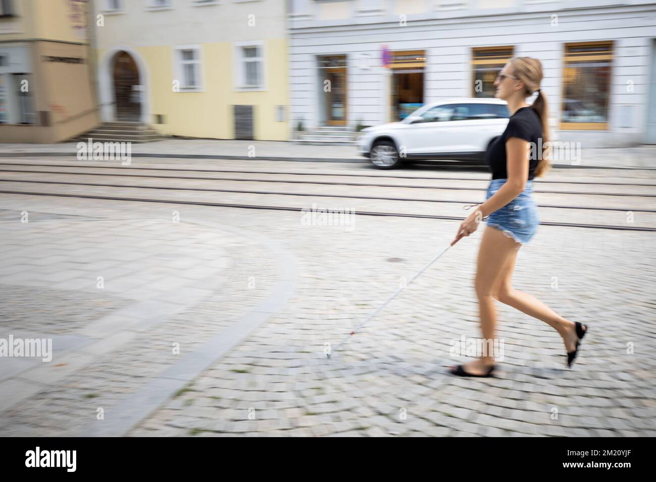 Blind woman walking on city streets, using her white cane to navigate ...