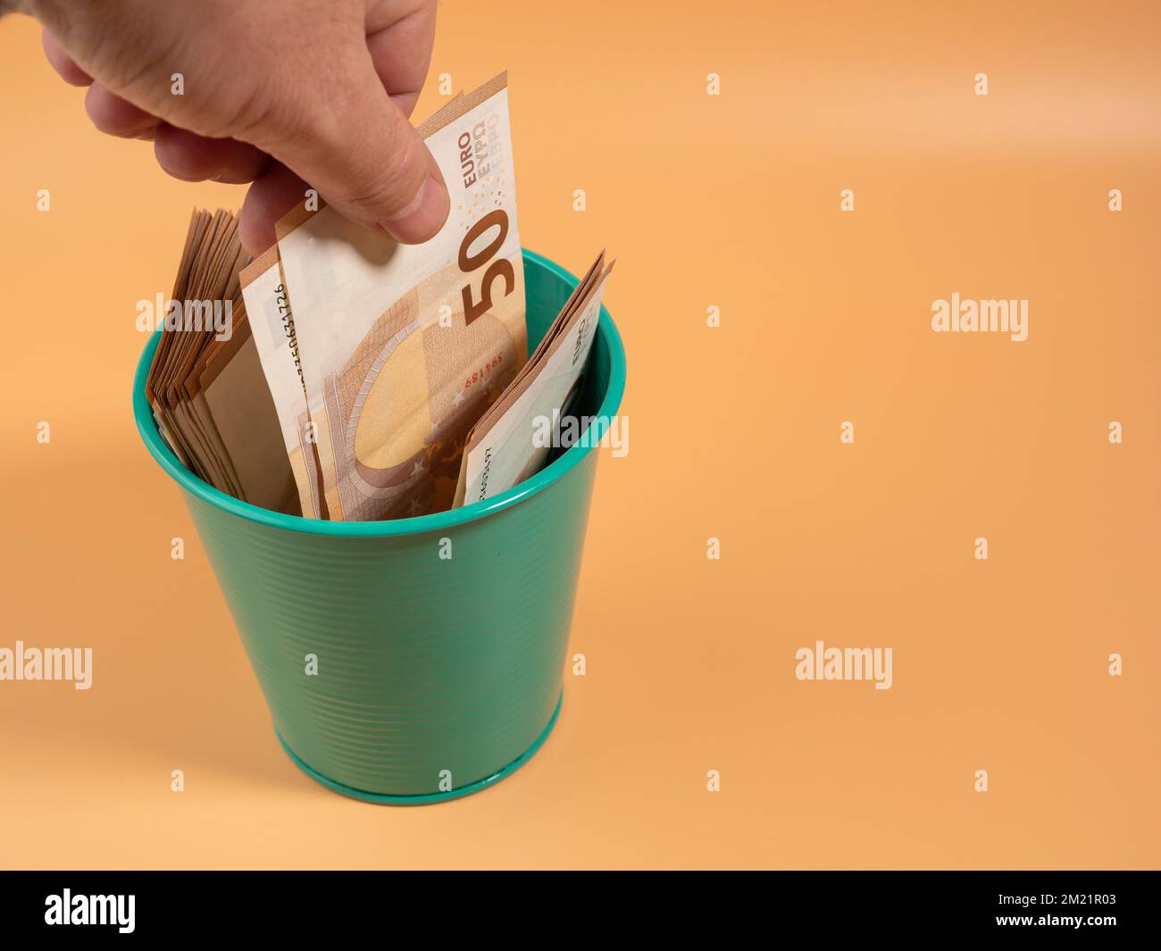 Money in the trash can on an orange background. Euros in the trash ...
