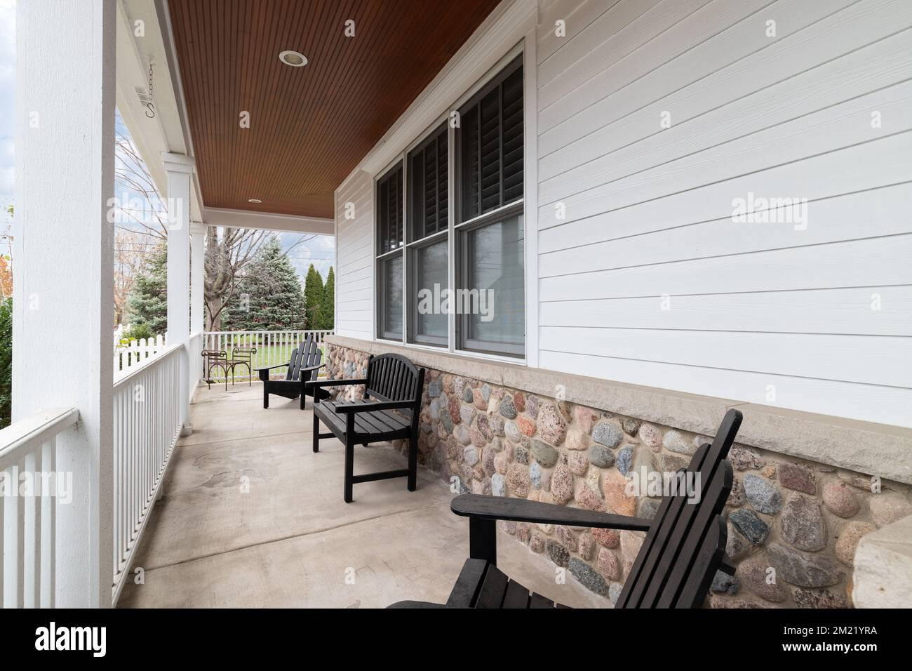 The wrap around front porch of a luxury home with white and rock siding ...