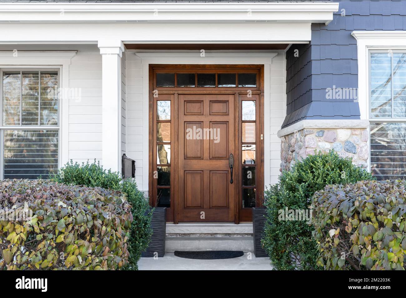 A wooden front door, surrounded by windows, with white, blue, and stone ...