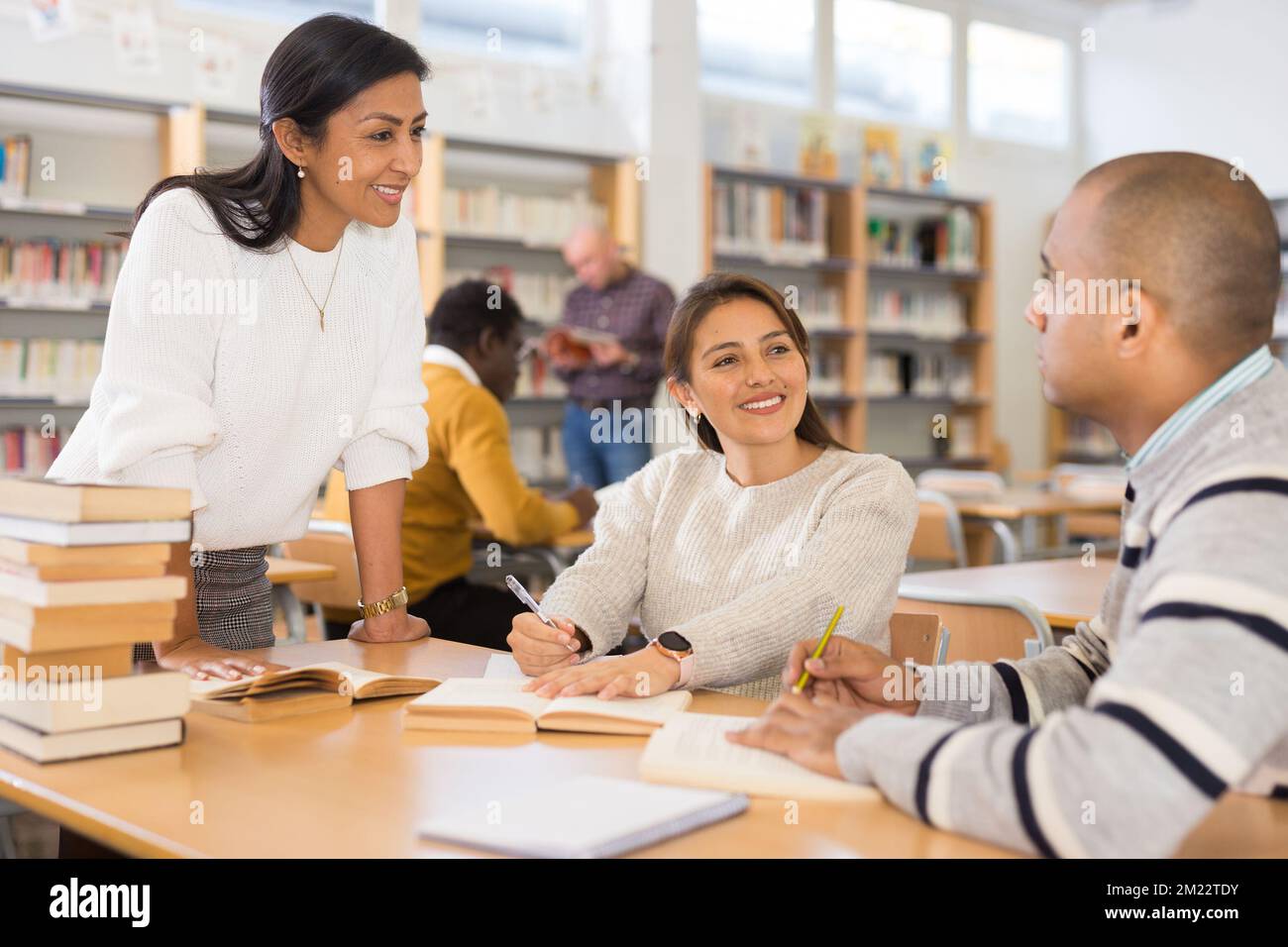 Group of positive adult hispanic students communicating in library ...
