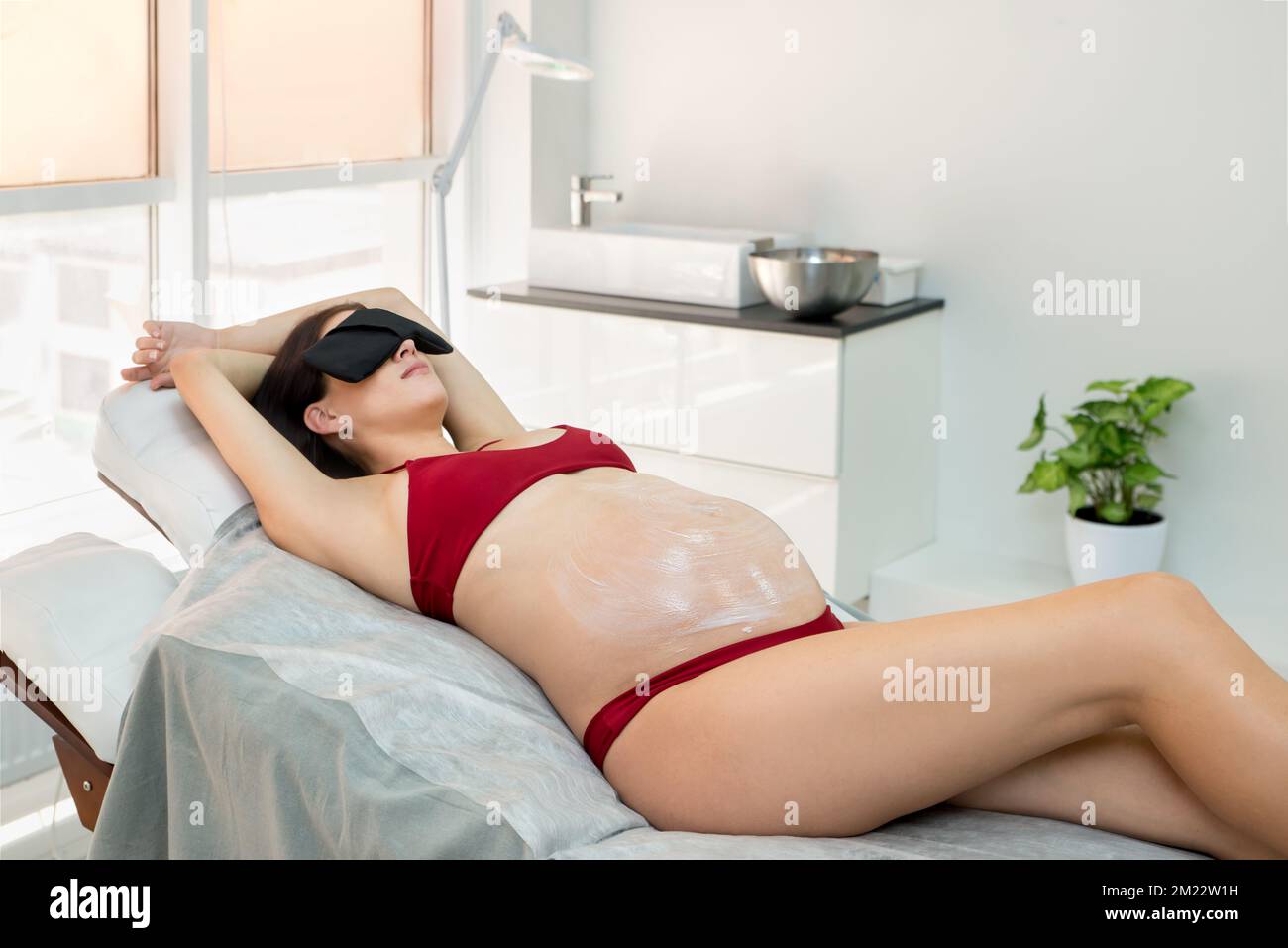 Beautiful young pregnant woman gets useful body care treatment in SPA salon. Model with big ...