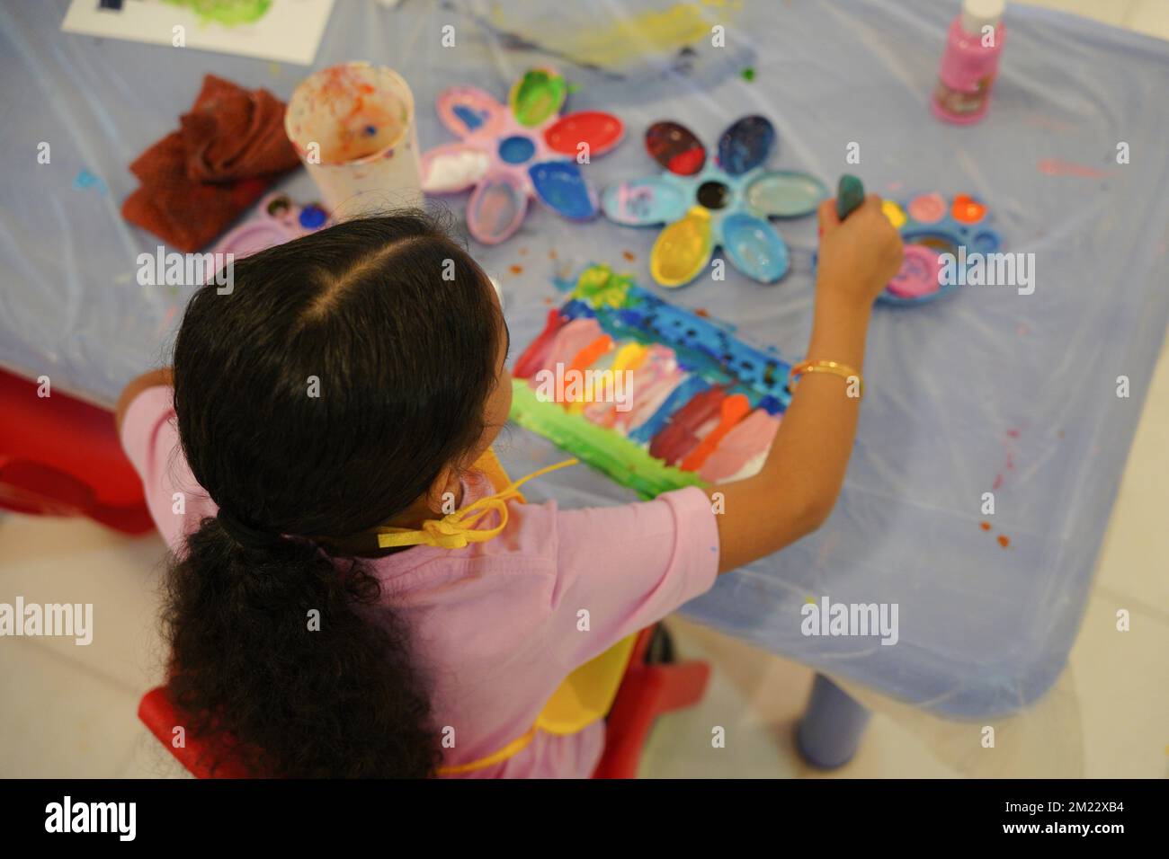Little girl painting with colourful paints using brushes and colour ...